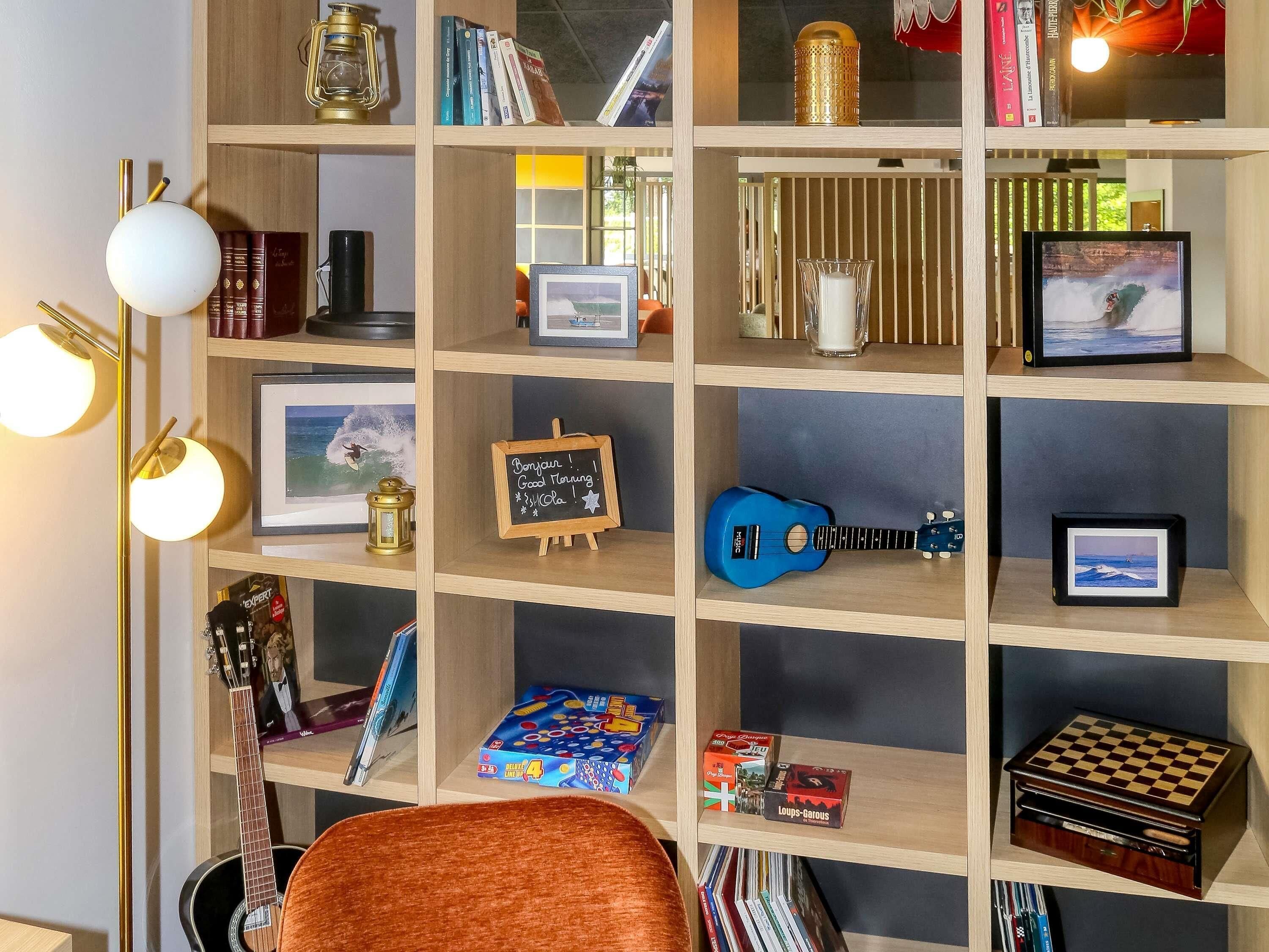 Uma estante com livros, um pequeno quadro negro, um ukulele azul e um tabuleiro de xadrez.