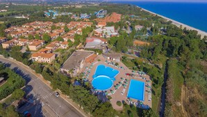 Vista aérea de um resort à beira-mar, com vários edifícios, uma grande piscina e uma praia.
