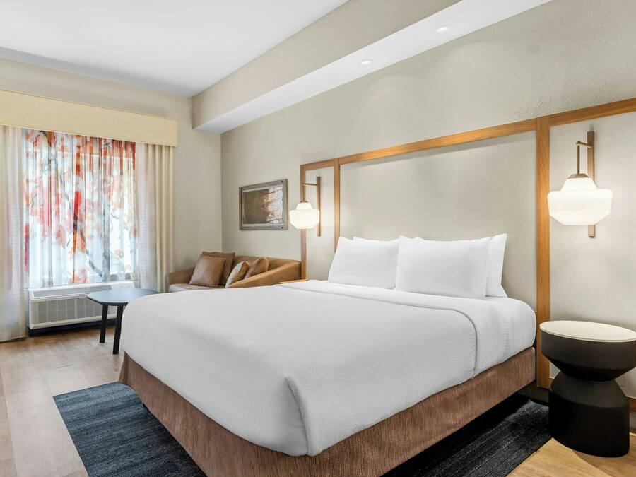 Quarto de hotel com uma cama grande, uma escrivaninha, uma cadeira e uma janela com cortinas.
