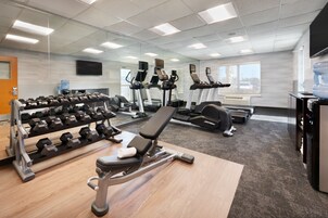 Academia com equipamentos de exercício, um banco e um bebedouro.