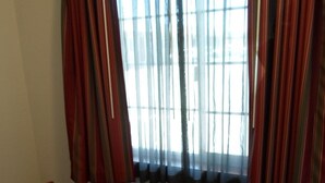 Uma mesa redonda de madeira com duas cadeiras, uma janela com cortinas e um aquecedor fixado na parede.