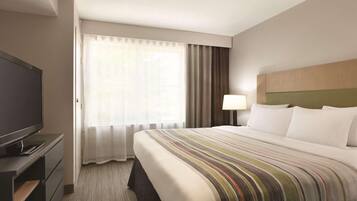 Quarto de hotel com cama, televisão, luminária e janela com cortinas.