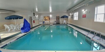 Piscina interna com água cristalina, rodeada por cadeiras brancas e guarda-sóis azuis.