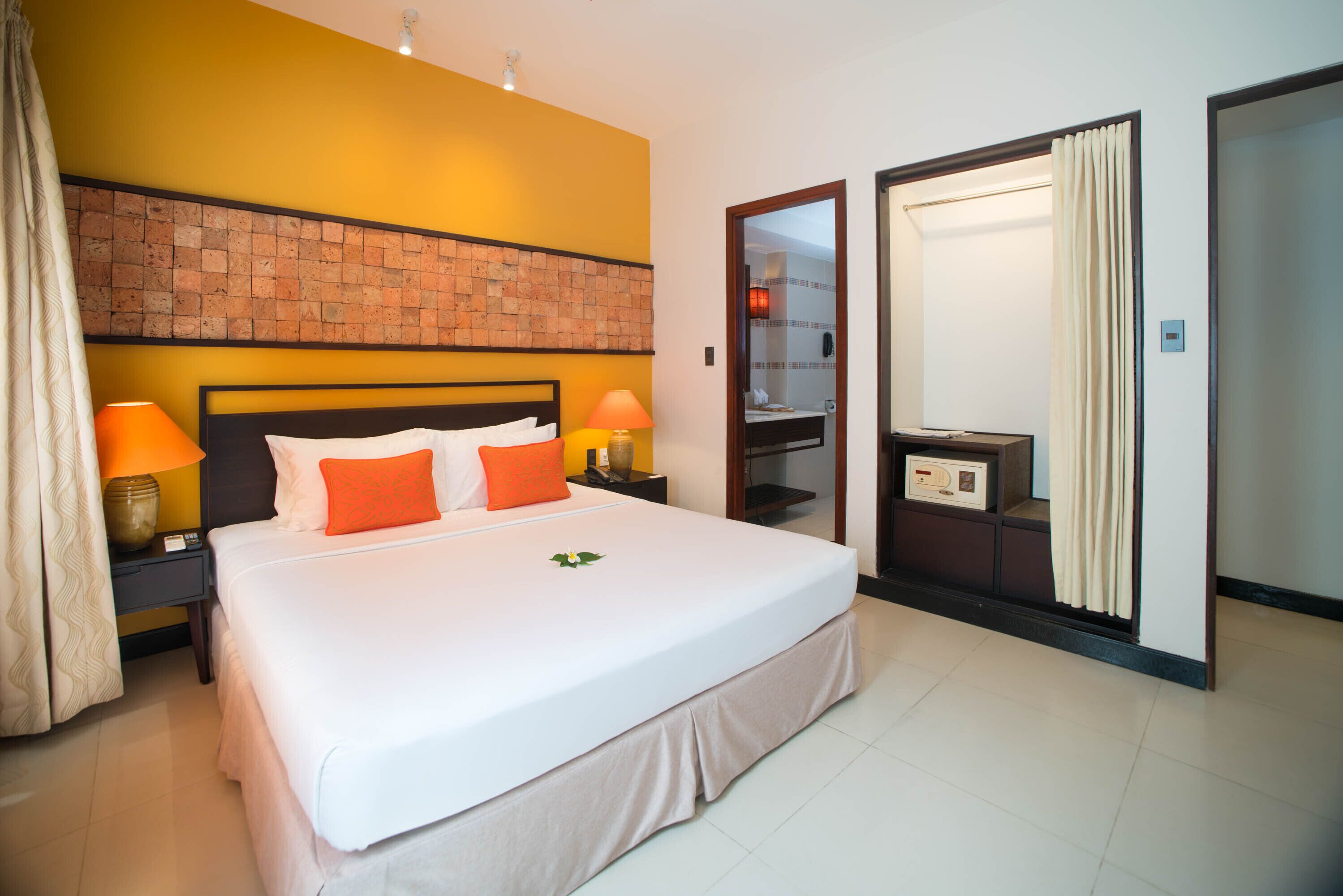 Quarto de hotel com uma cama grande, duas luminárias de cabeceira, parede de tijolos decorativa, um espelho e um guarda-roupa.