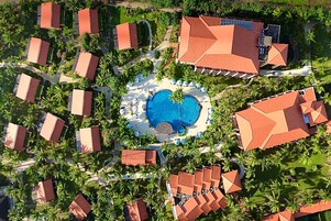 Vista aérea de um resort com uma piscina central, várias construções estilo bangalô e palmeiras.