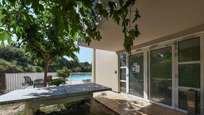 Um pátio com mesa, piscina e uma casa com portas de correr.