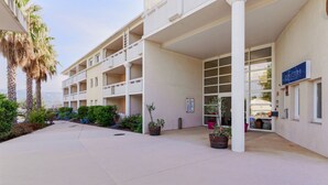 Um hotel moderno com área externa coberta, várias varandas e plantas em vasos.