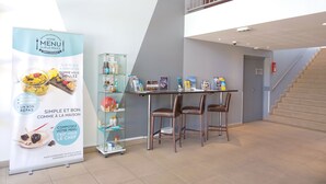 Um hall de hotel moderno com uma receção, uma vitrine de vidro e uma escadaria.