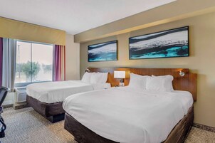 Quarto de hotel com duas camas, uma janela grande com cortinas e duas pinturas abstratas na parede.