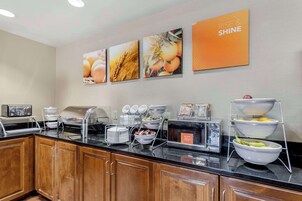 Uma mesa de buffet para o café da manhã com diversas opções de alimentos e um canto para café.