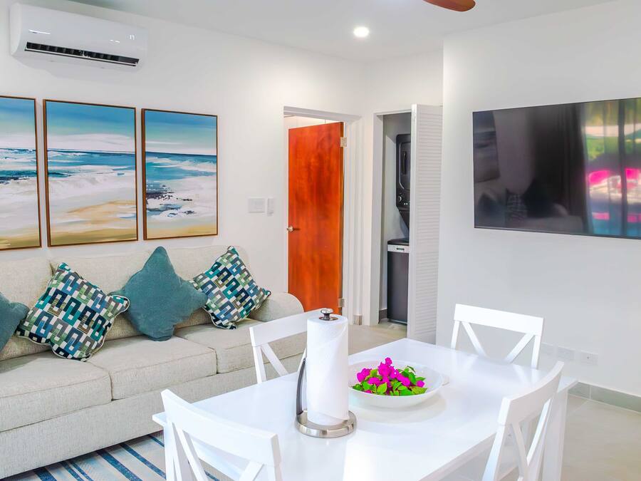 Uma sala de estar moderna com um sofá, uma mesa de jantar com cadeiras, uma televisão e obras de arte nas paredes.