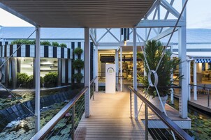 Uma galeria coberta com vista para um corpo d'água, uma placa com o nome 'Oak Vine' e uma planta em vaso.