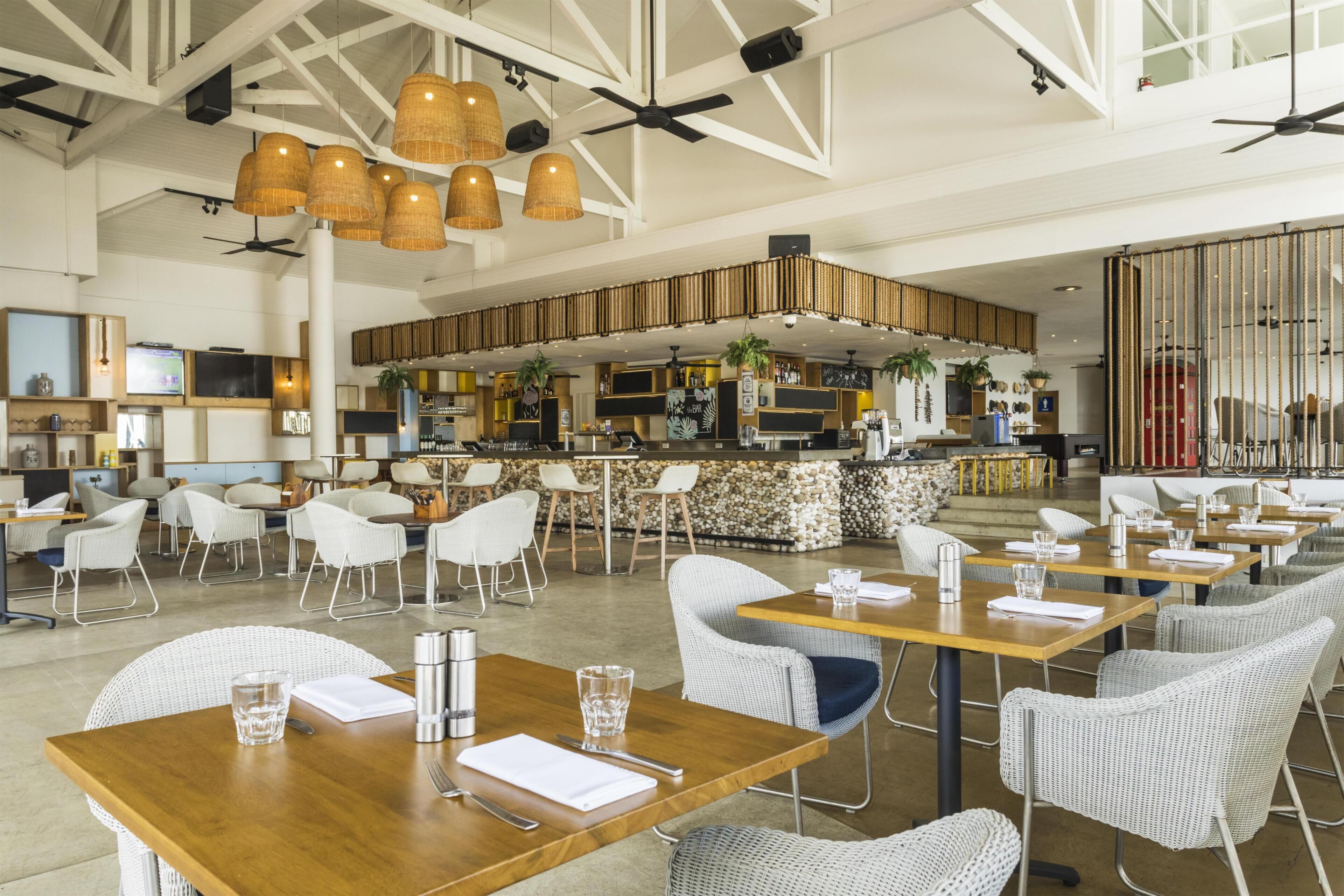 Um restaurante espaçoso com tetos altos, luminárias pendentes de vime e um espaço de bar.