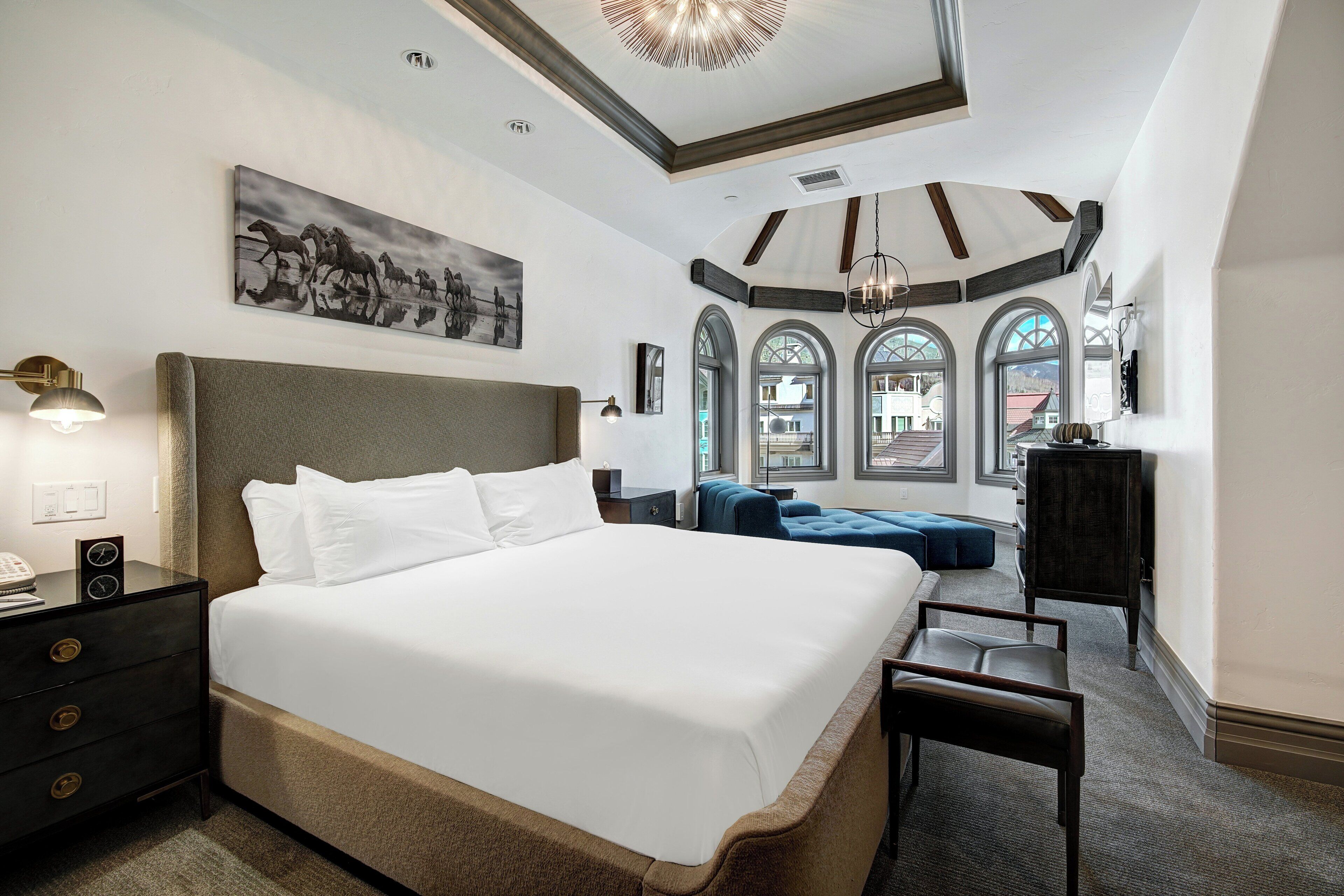 Quarto de hotel com uma cama grande, uma mesa, uma cadeira e vista através de janelas em arco.