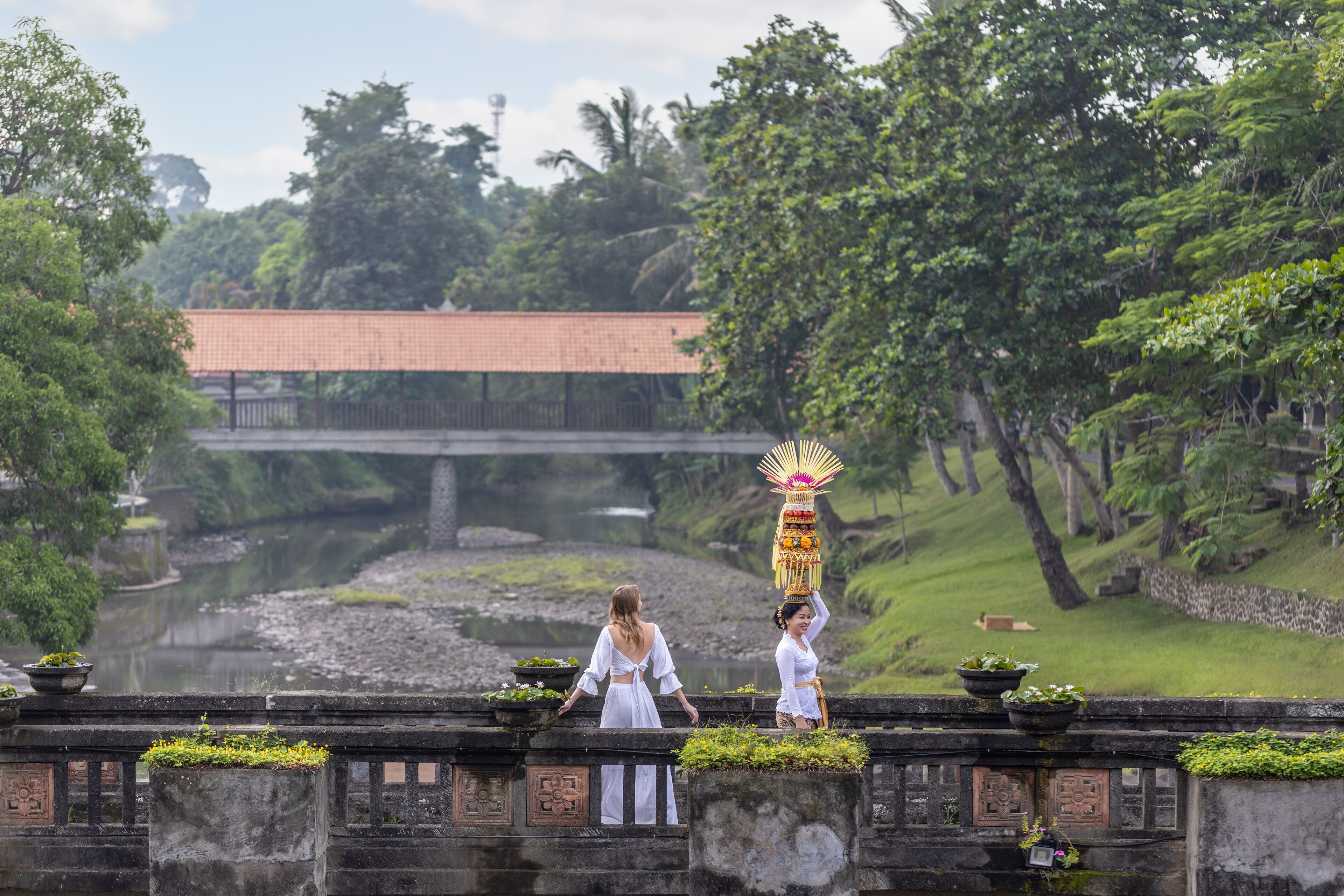 Uma ponte sobre um rio, com vegetação e uma construção tradicional.