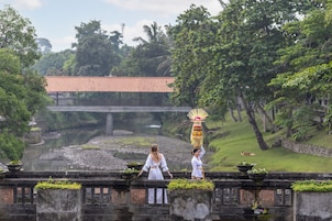 Uma ponte sobre um rio, com vegetação e uma construção tradicional.