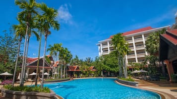 Área de piscina do resort com palmeiras, espreguiçadeiras e um prédio com telhado vermelho.