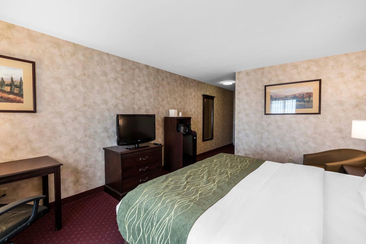 Quarto de hotel com cama, escrivaninha, televisão, máquina de café e duas fotos emolduradas nas paredes.