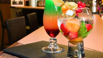Dois cocktails sobre uma mesa, com um bar ao fundo.