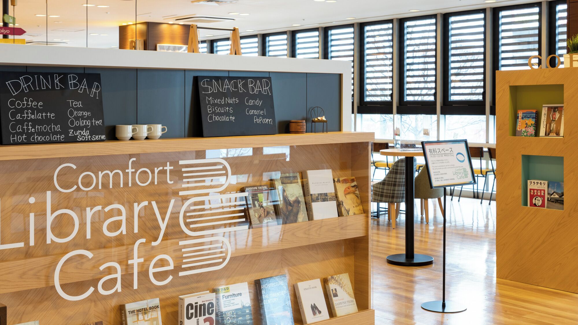 Café em biblioteca com balcão de bebidas, estantes de livros e área de estar.