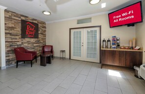 Lobby de um Red Roof Inn com parede de pedra, cadeiras de couro vermelho, balcão de recepção e uma placa indicando "Wi-Fi Grátis em Todos os Quartos".