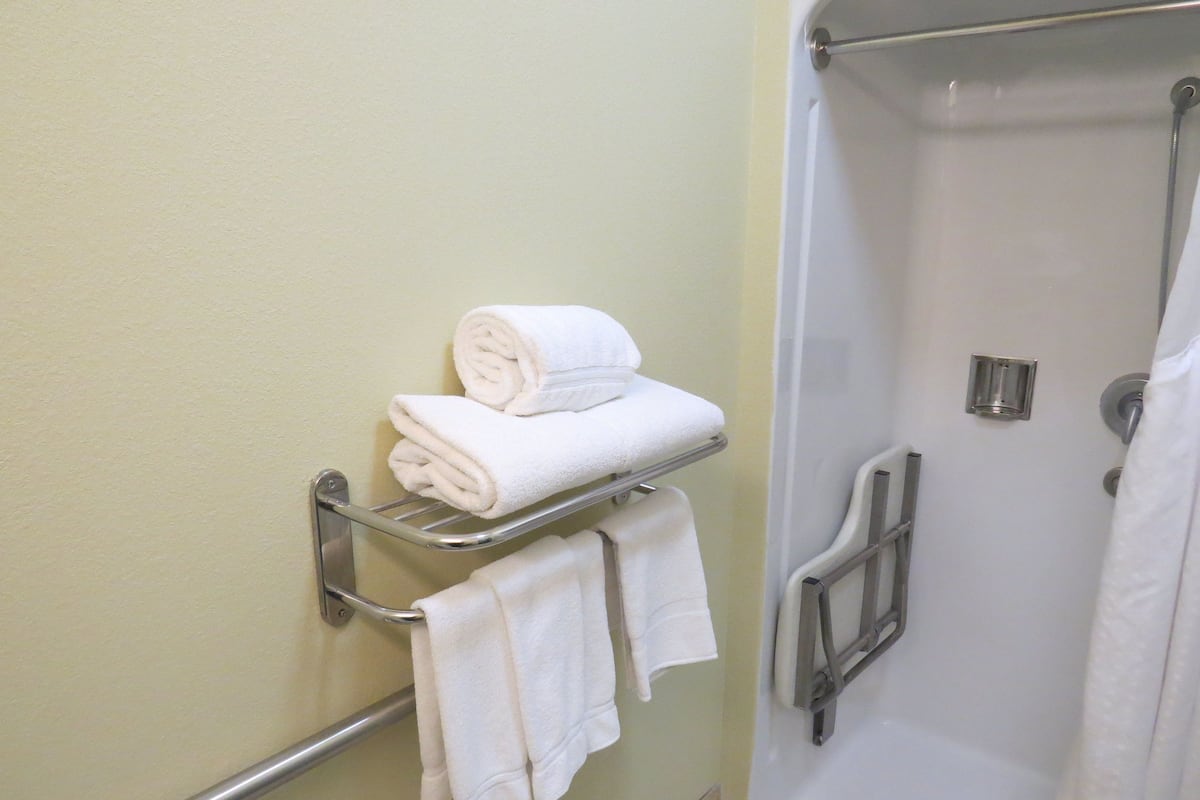 Casa de banho com porta-toalhas com toalhas dobradas, zona de duche com barra de apoio e candeeiro fixado na parede.