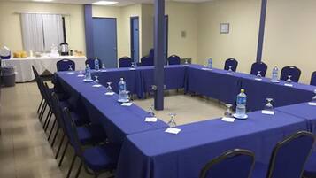 Uma sala de conferências com uma mesa comprida, cadeiras e garrafas de água.