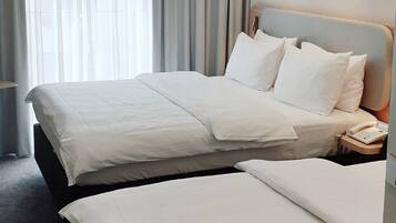 Quarto de hotel com uma cama grande, mesa de cabeceira com telefone e janela com cortinas.