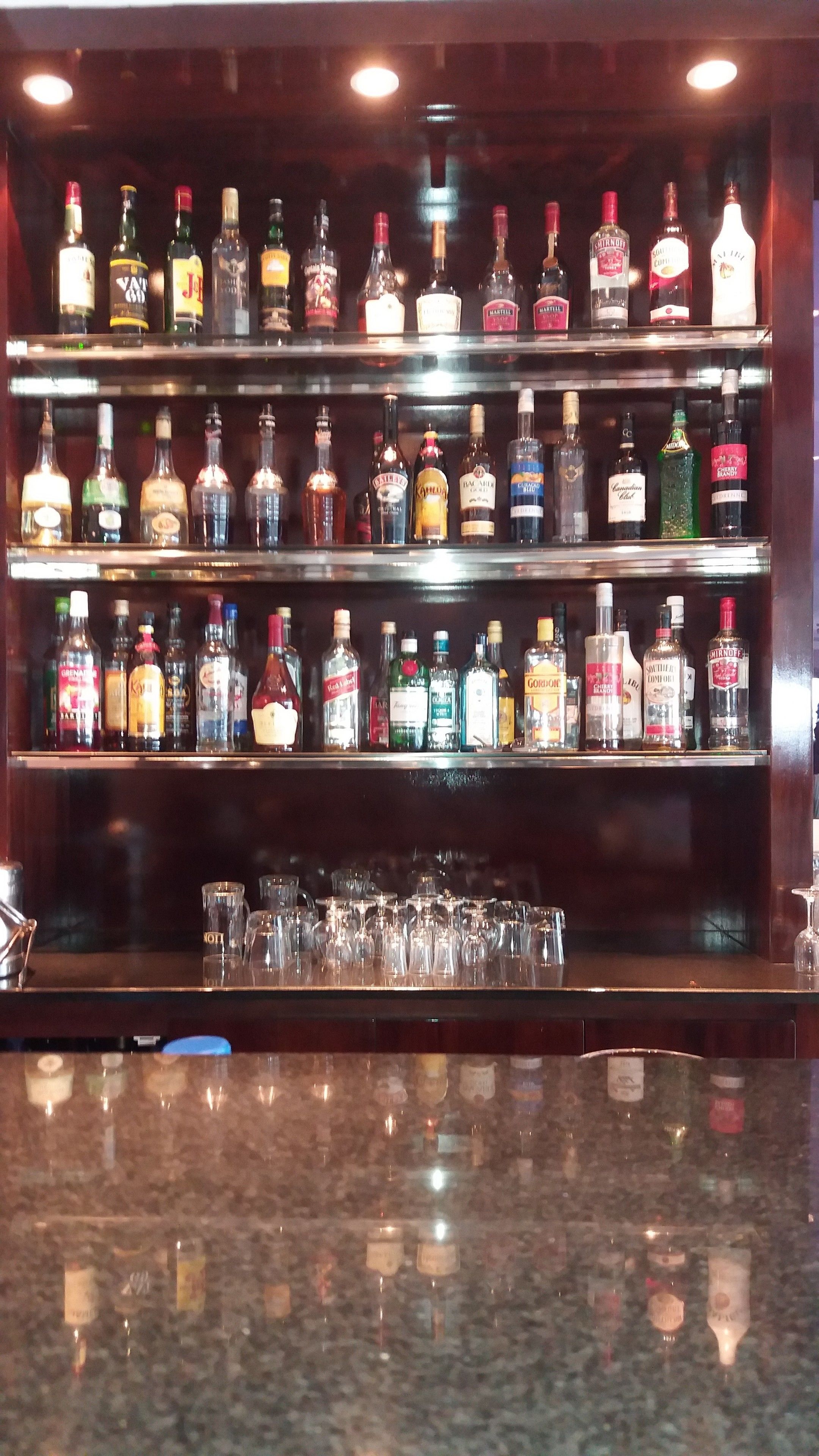 Um bar com várias prateleiras de garrafas de bebidas e copos.