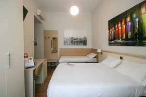 Quarto de hotel com duas camas, uma escrivaninha, uma cadeira, um quadro na parede e um ar condicionado.