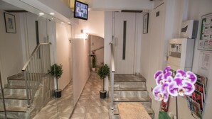 Um hall de hotel com piso de mármore, balcão de recepção, escada e plantas em vasos.