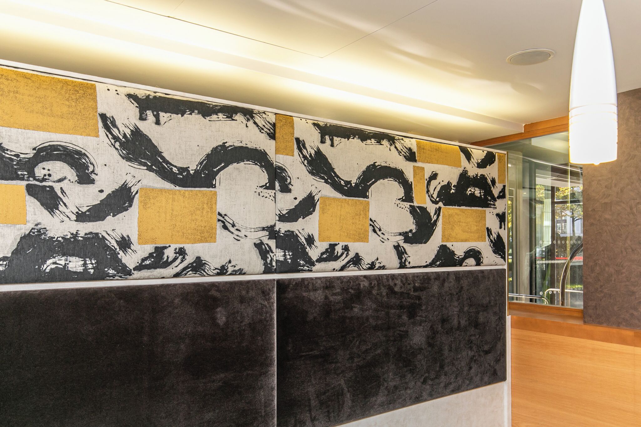 Um interior moderno com uma grande obra de arte abstrata na parede, uma parede texturizada semelhante a mármore e uma porta de vidro que dá para um corredor.