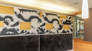 Um interior moderno com uma grande obra de arte abstrata na parede, uma parede texturizada semelhante a mármore e uma porta de vidro que dá para um corredor.