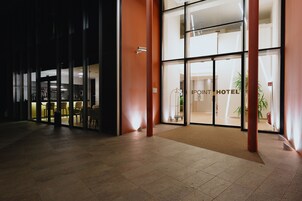 Entrada de um hotel com fachada de vidro, balcão de recepção e espaço interior com assentos.