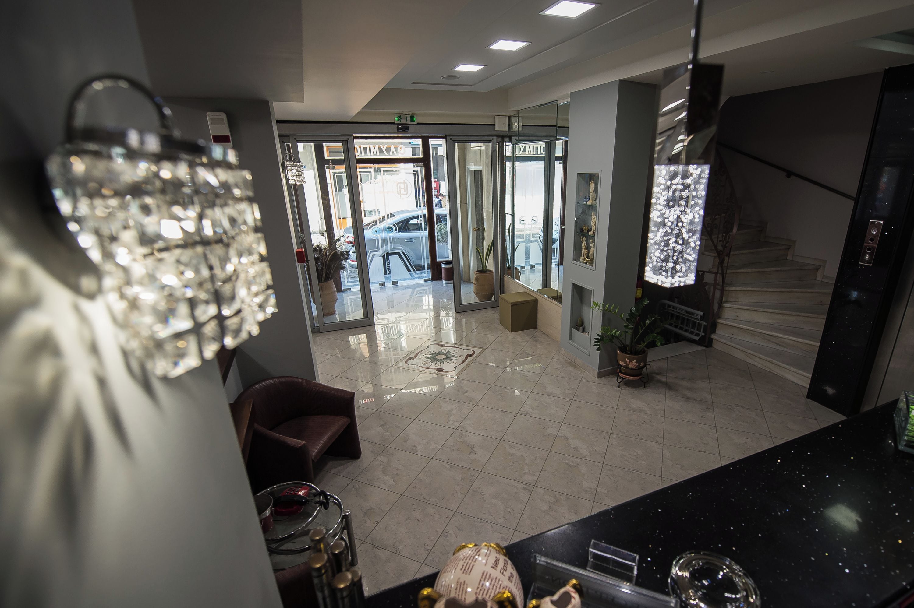 Um saguão de hotel com uma mesa de recepção, uma área de estar e vista para a rua através das portas de entrada.