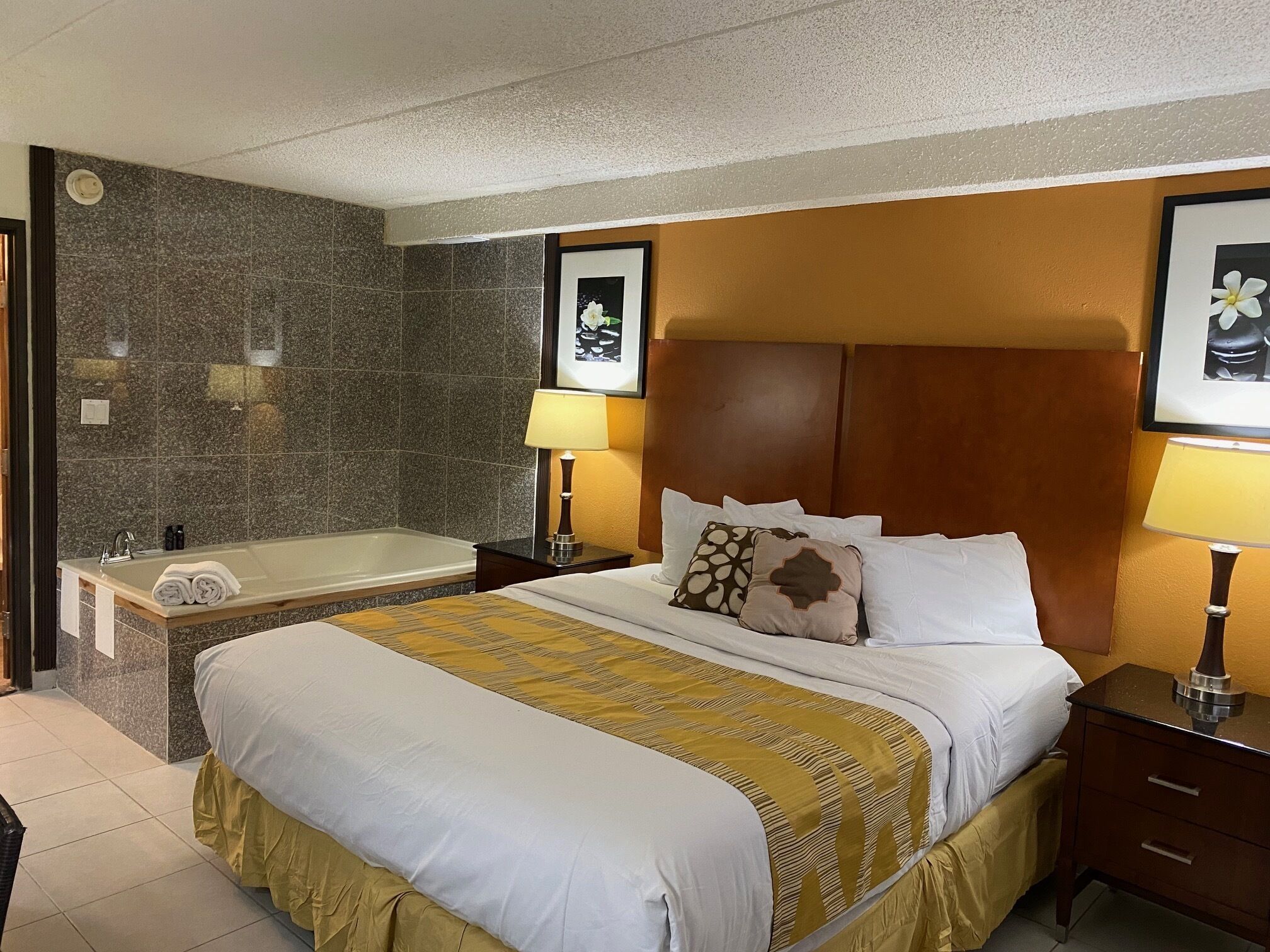 Quarto de hotel com uma cama grande, banheiro privativo com banheira e duas luminárias de cabeceira.