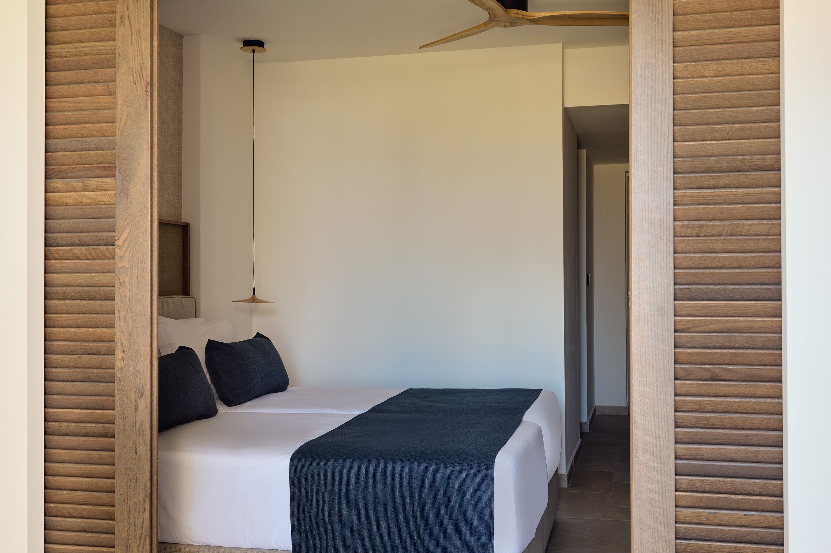 Quarto com cama, almofadas, mesa de cabeceira e luminária pendente.