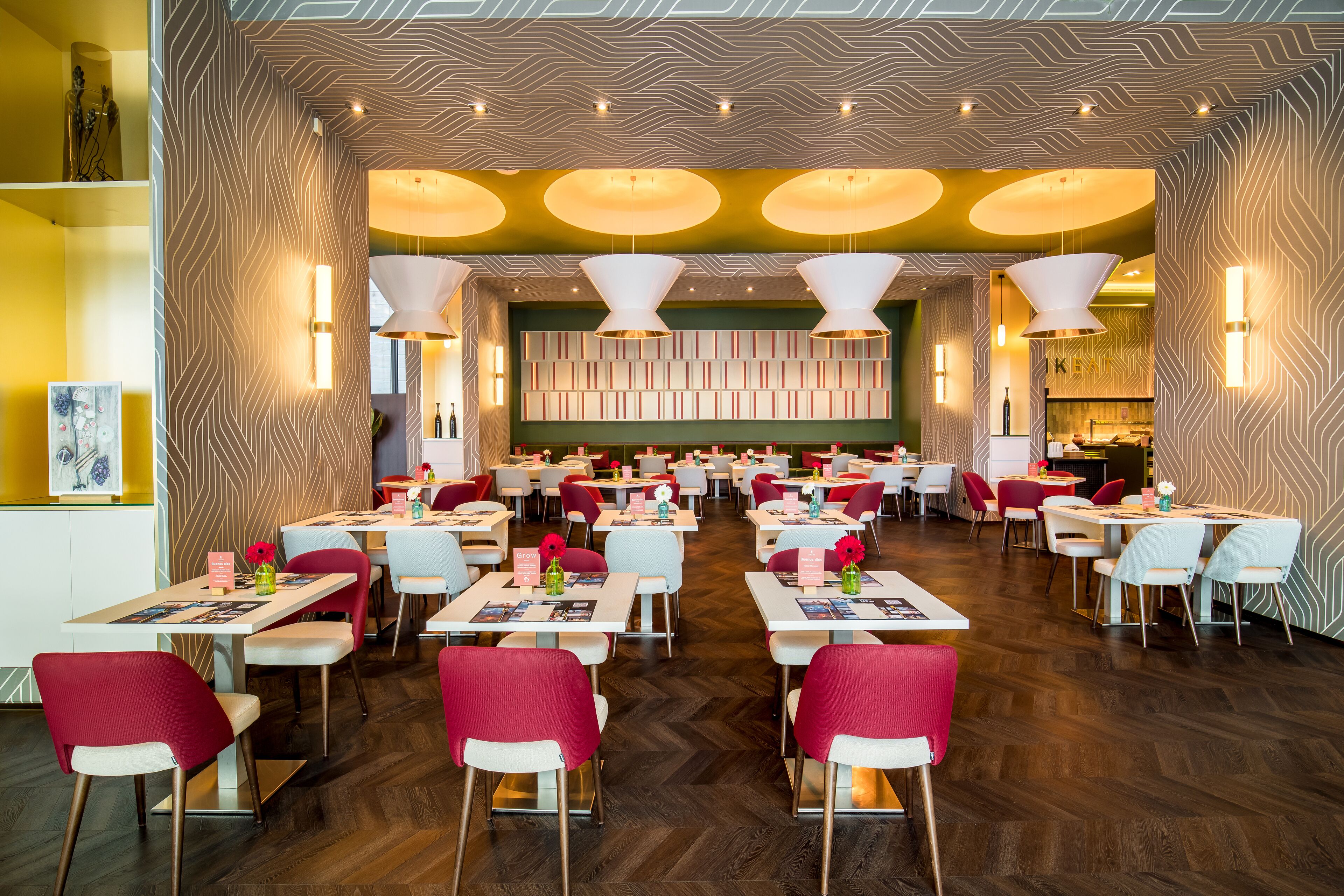 Um restaurante espaçoso com várias mesas e cadeiras, apresentando um papel de parede estampado e iluminação pendente moderna.