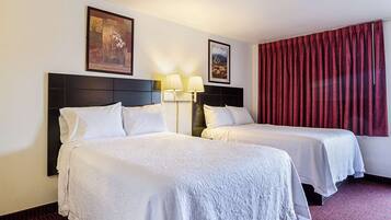 Quarto de hotel com duas camas, cabeceira, luminárias fixadas na parede e uma janela grande com cortinas vermelhas.
