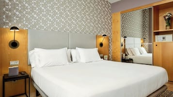 Quarto de hotel com uma cama grande, uma mesinha de cabeceira, um espelho e um guarda-roupa.