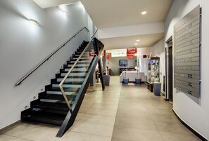 Um interior moderno com escadaria de vidro, balcão de recepção e um diretório fixado na parede.