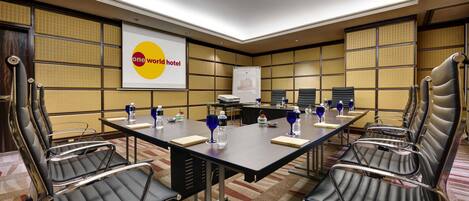 Uma sala de conferências com uma mesa comprida, quatro cadeiras e uma tela de projeção exibindo o logotipo do Hotel One World.