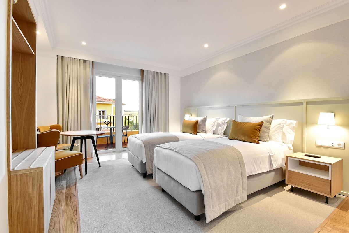 Quarto de hotel com duas camas, uma escrivaninha e vista para o exterior.