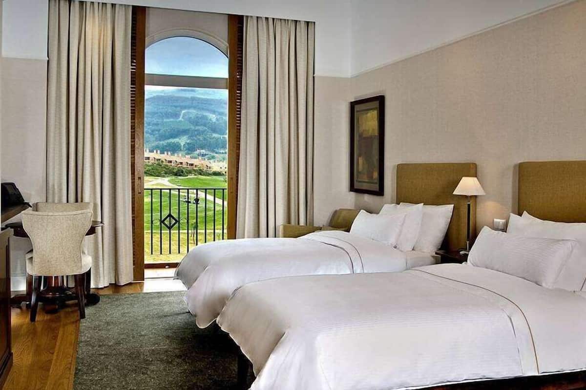 Quarto de hotel com duas camas, uma escrivaninha, uma cadeira e vista para um campo de golfe.