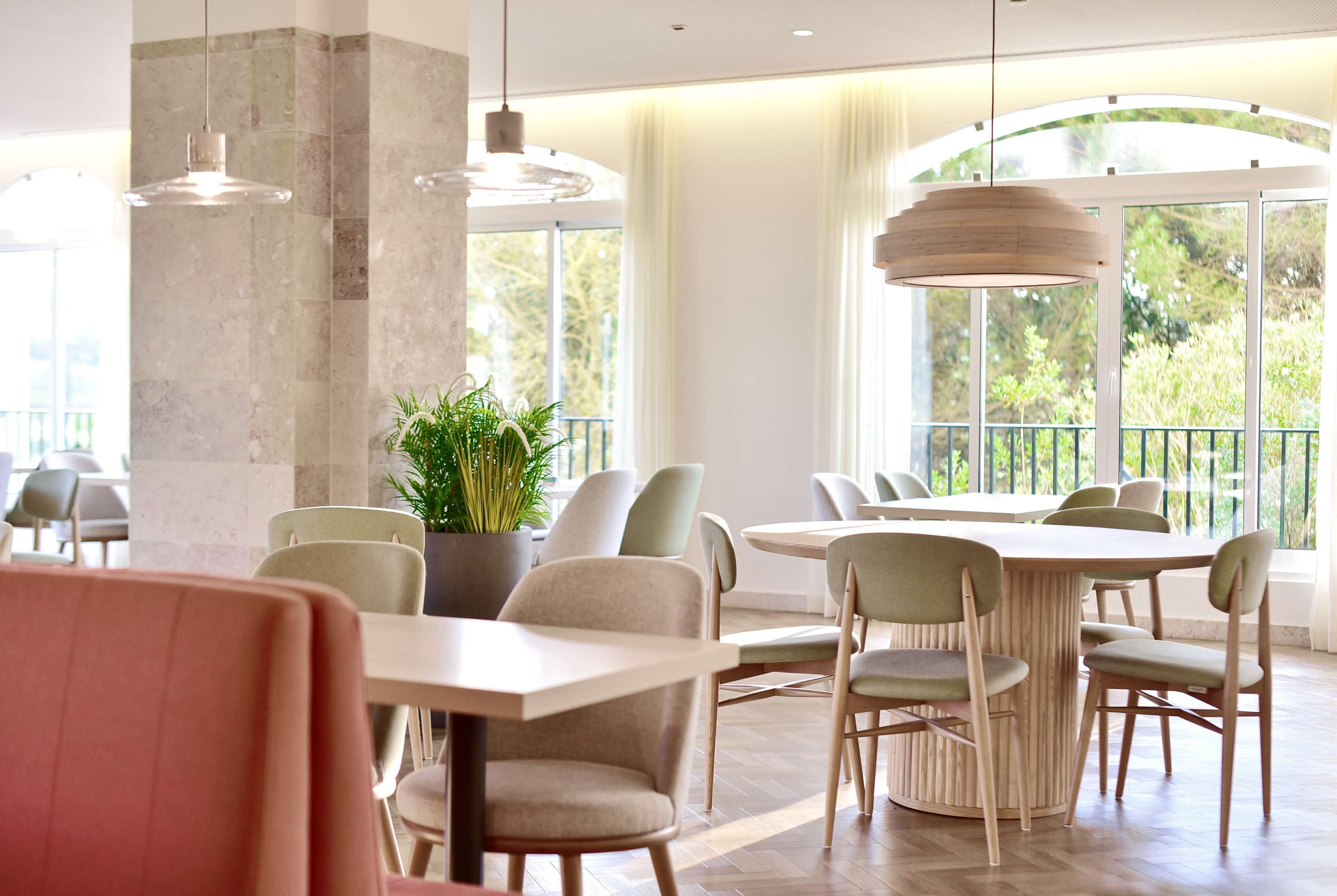 Uma área de jantar moderna com uma mesa redonda e cadeiras, janelas amplas com vista para o verde e iluminação pendente.