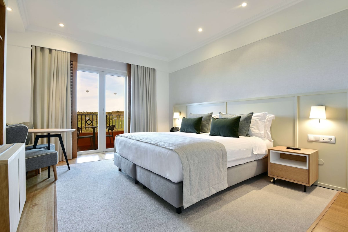Quarto de hotel moderno com uma cama grande, uma escrivaninha e vista para o exterior.