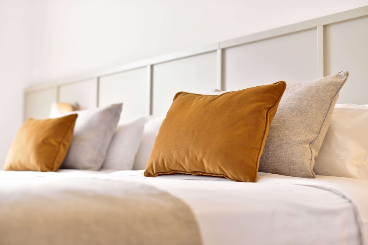 Uma cama com várias almofadas e cabeceira.
