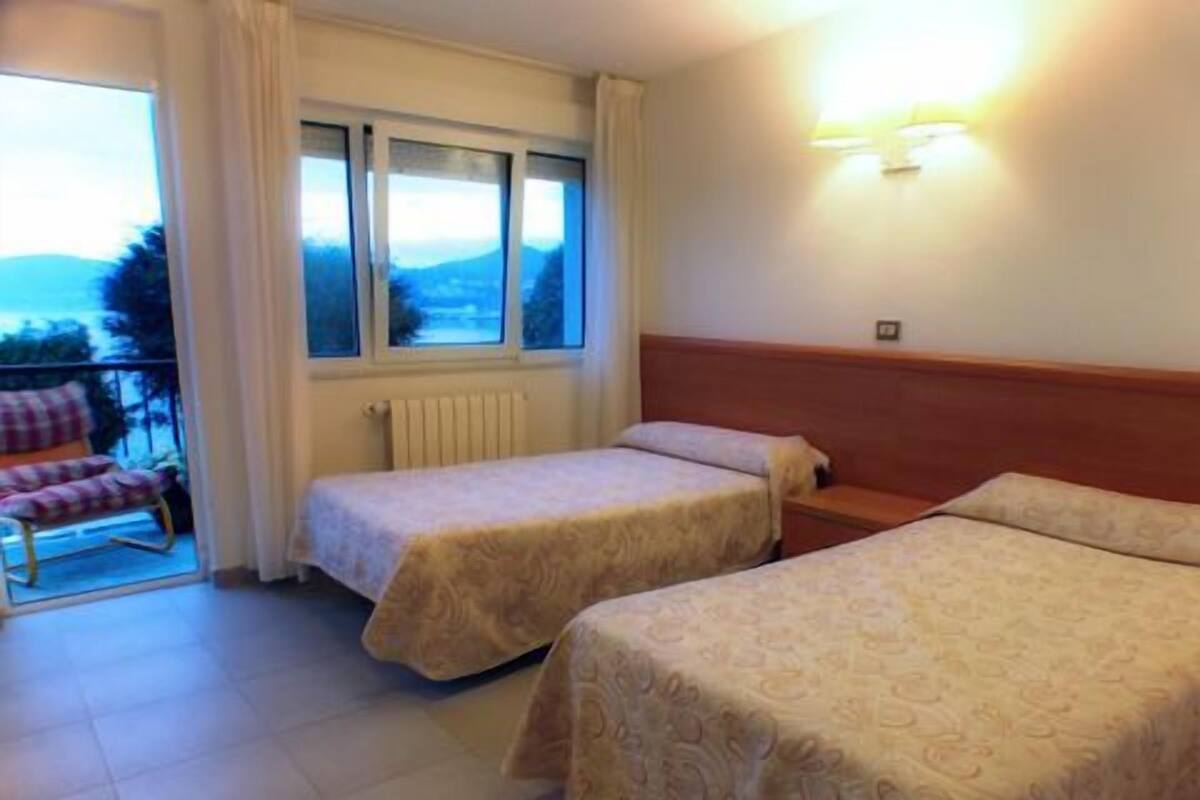 Quarto de hotel com duas camas, uma janela com vista, uma cadeira junto à janela e um radiador.