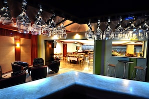 Uma área de bar com bancada de mármore, copos de vinho pendurados e um espaço de estar com cadeiras e mesas.