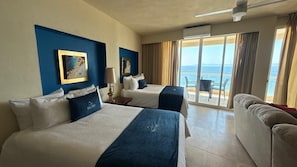Quarto de hotel com duas camas, um sofá, uma mesa de jantar e vista para o mar.